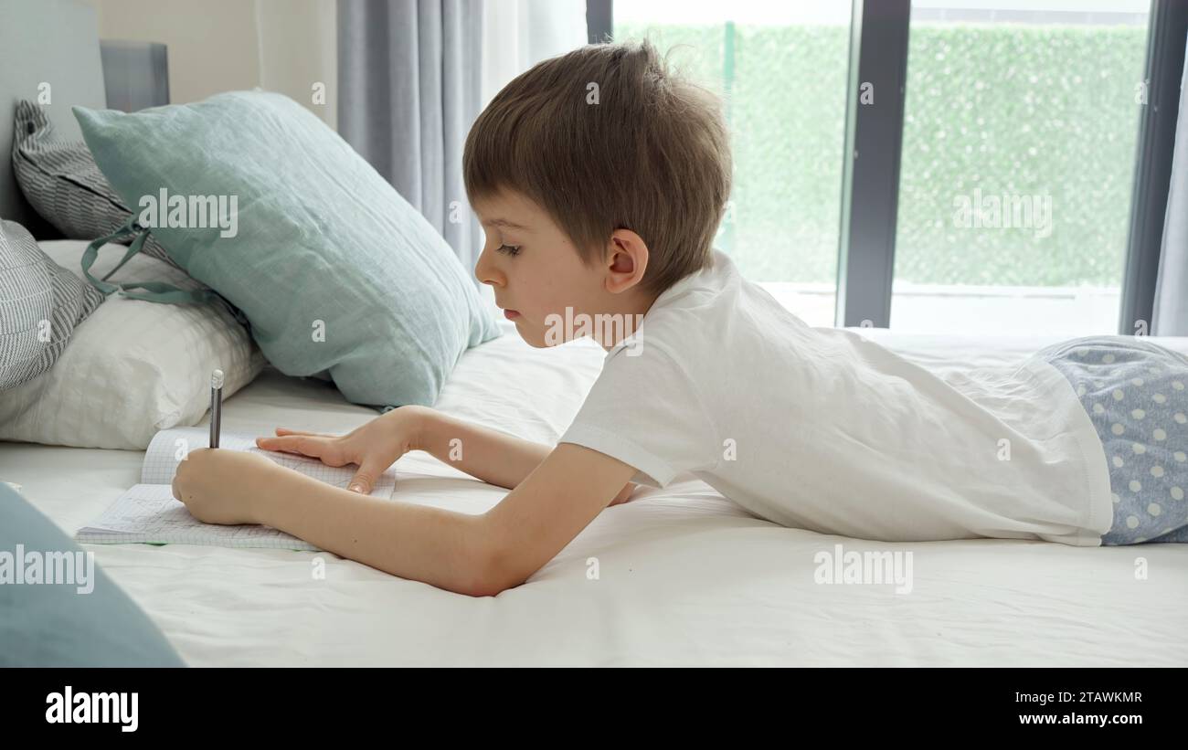 Little boy wearing pajamas doing homework in bed after waking up in ...