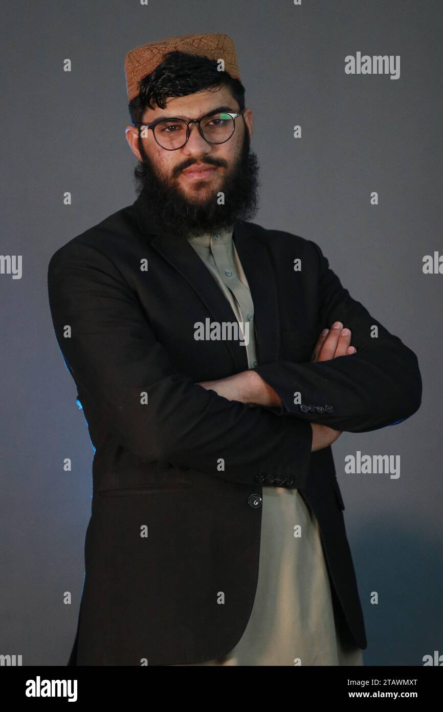 A young Muslim man with a beard standing against a gray background ...