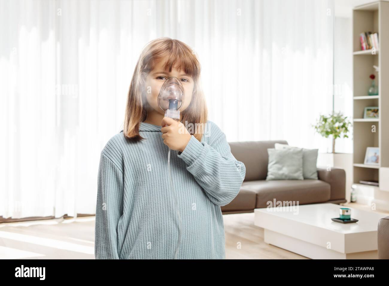 Little girl using an inhaler mask with vapor mist at home in a living ...
