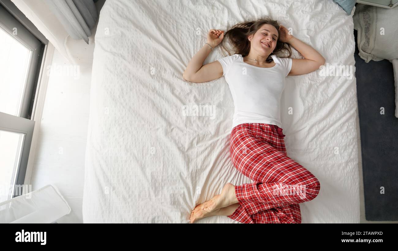 Young woman in pajamas lying on a bed with a big smile near a large ...