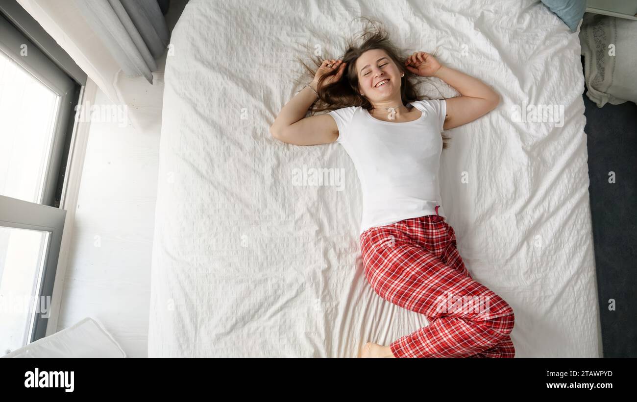 Smiling young woman in cozy pajamas falling onto a soft bed near a ...