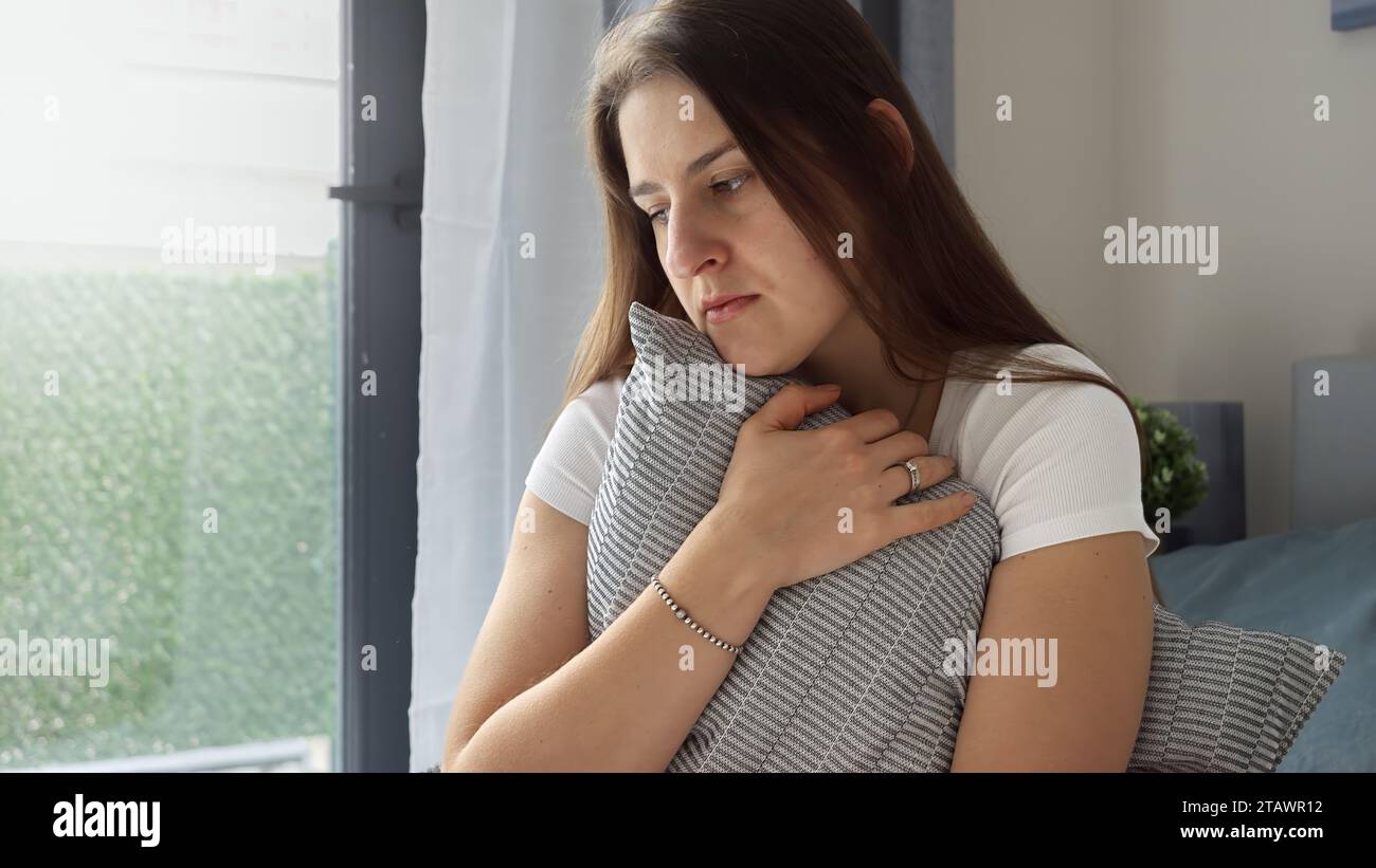 With tears in her eyes, the young woman sits on the bed, her arms ...