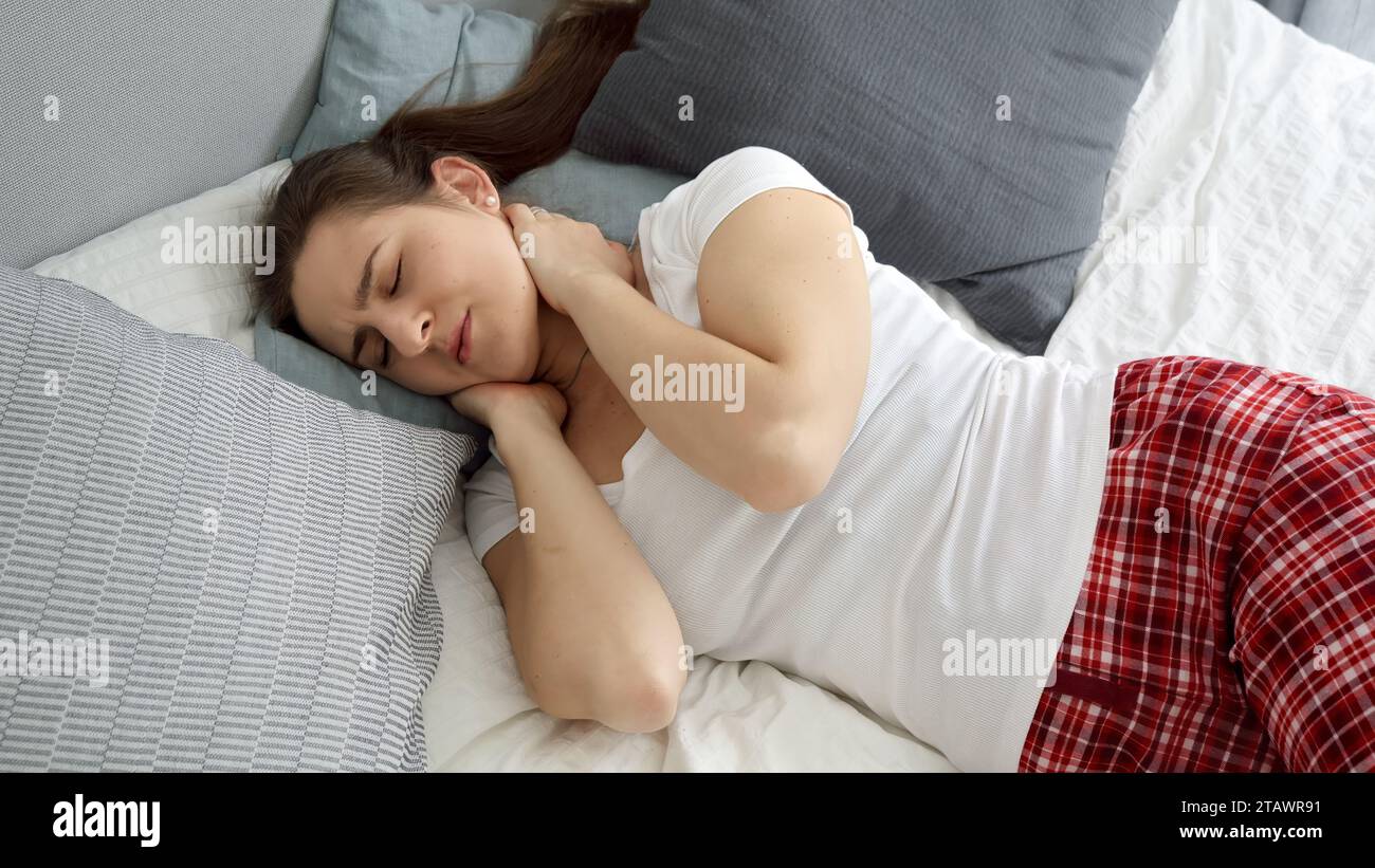 Young woman feeling pain in neck and massaging muscles after sleeping on uncomfortable bed Stock ...