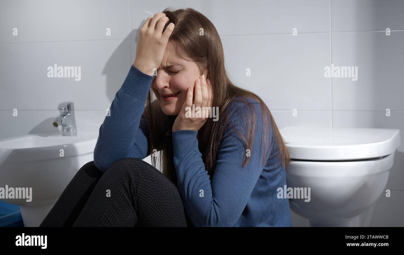 Crying woman suffering from depression sitting on floor in bathroom at ...