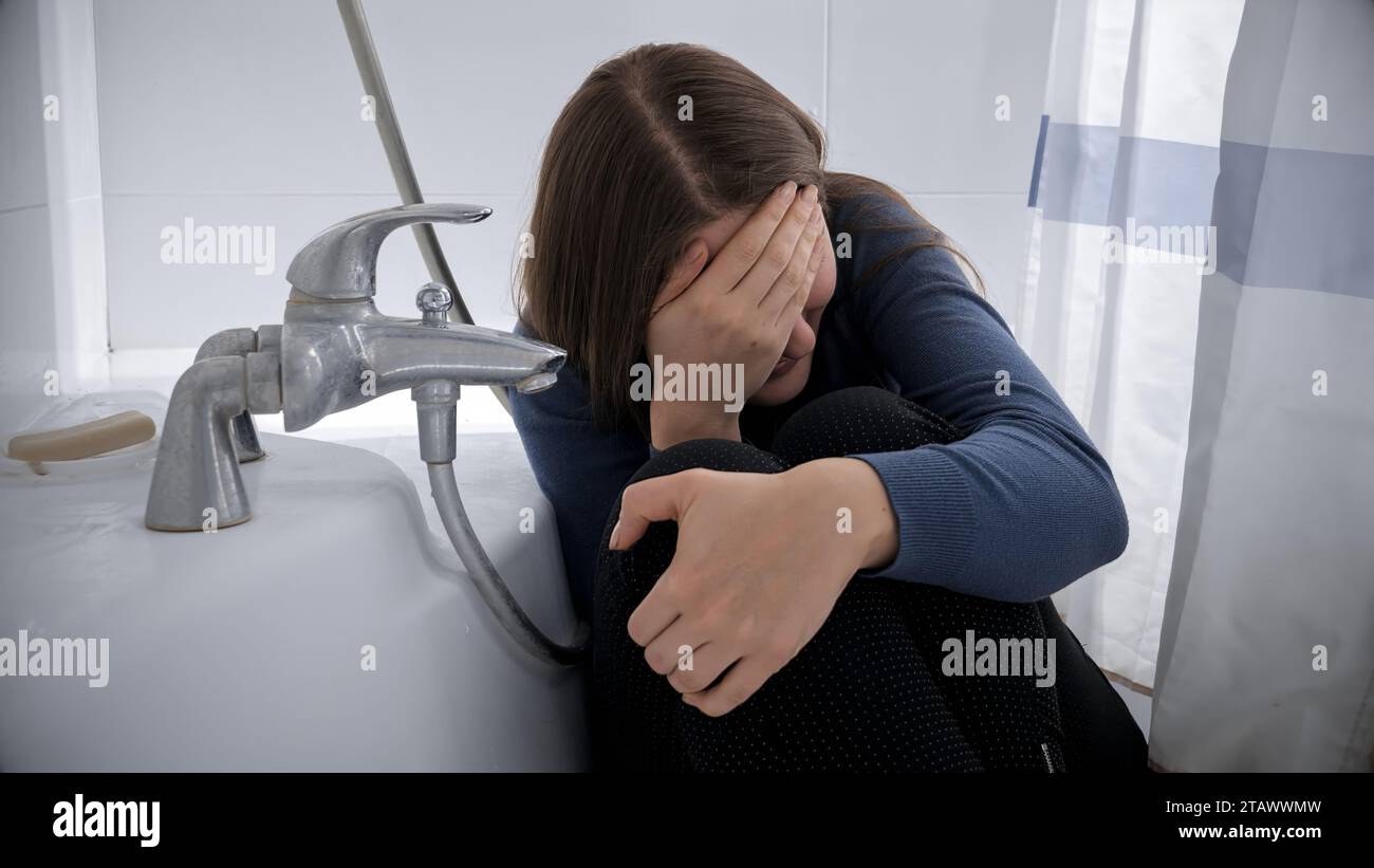 Upset crying woman sitting in bath after being victim of abuse or ...