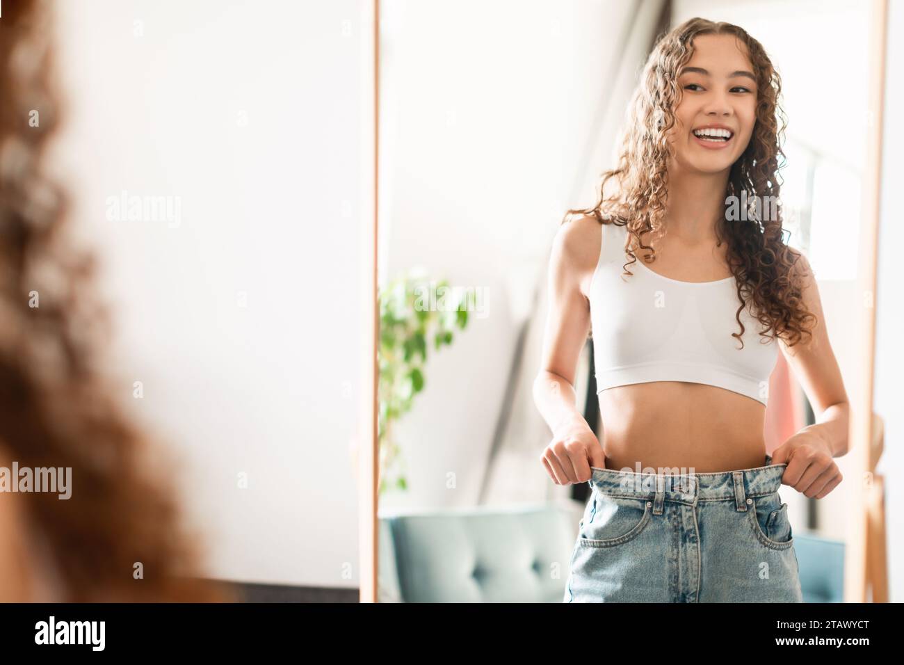 Happy teen girl comparing slimmed waist in mirror at home Stock Photo ...