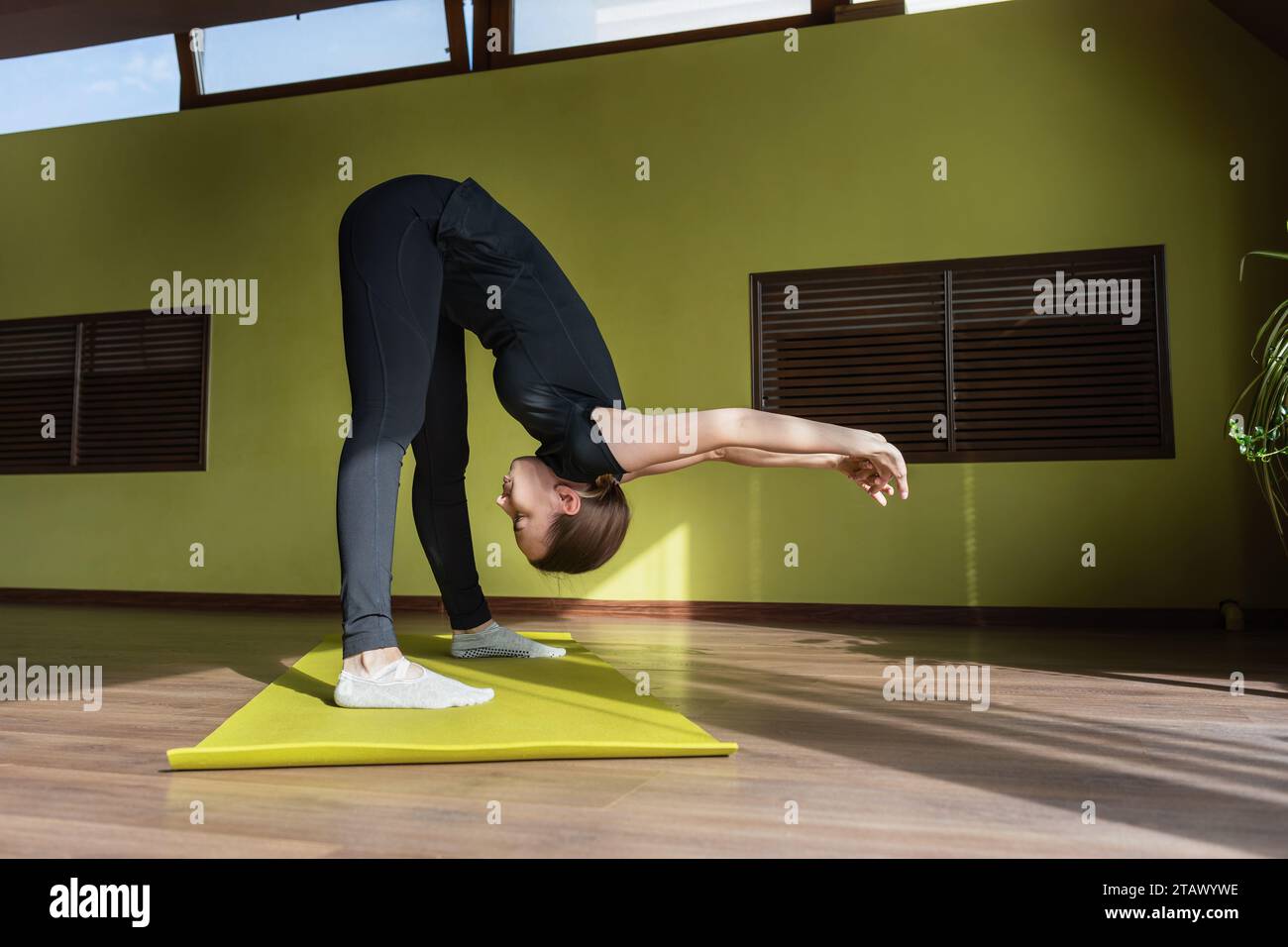 Young woman performing Dandayamana Mudrasana exercise, forward bend ...