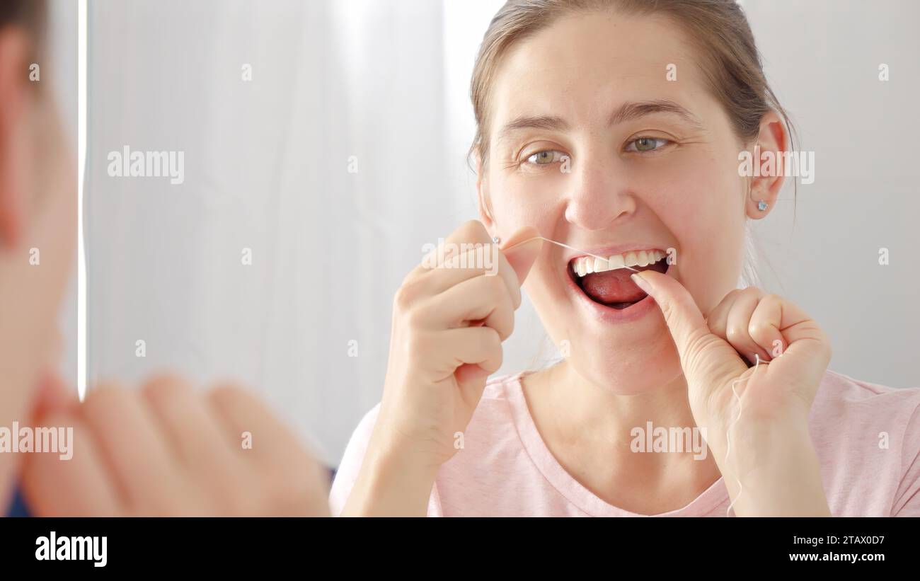 Closeup portrait of young woman using dental floss to clean her teeth ...
