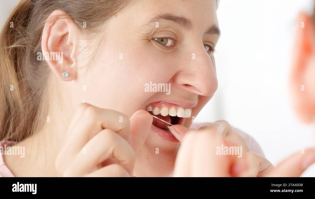 Young woman using dental floss to clean stuck food out of her teeth ...