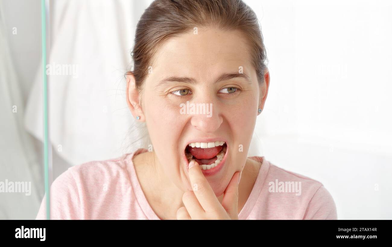 Beautiful young woman looking in the mirror and checking her teeth with ...