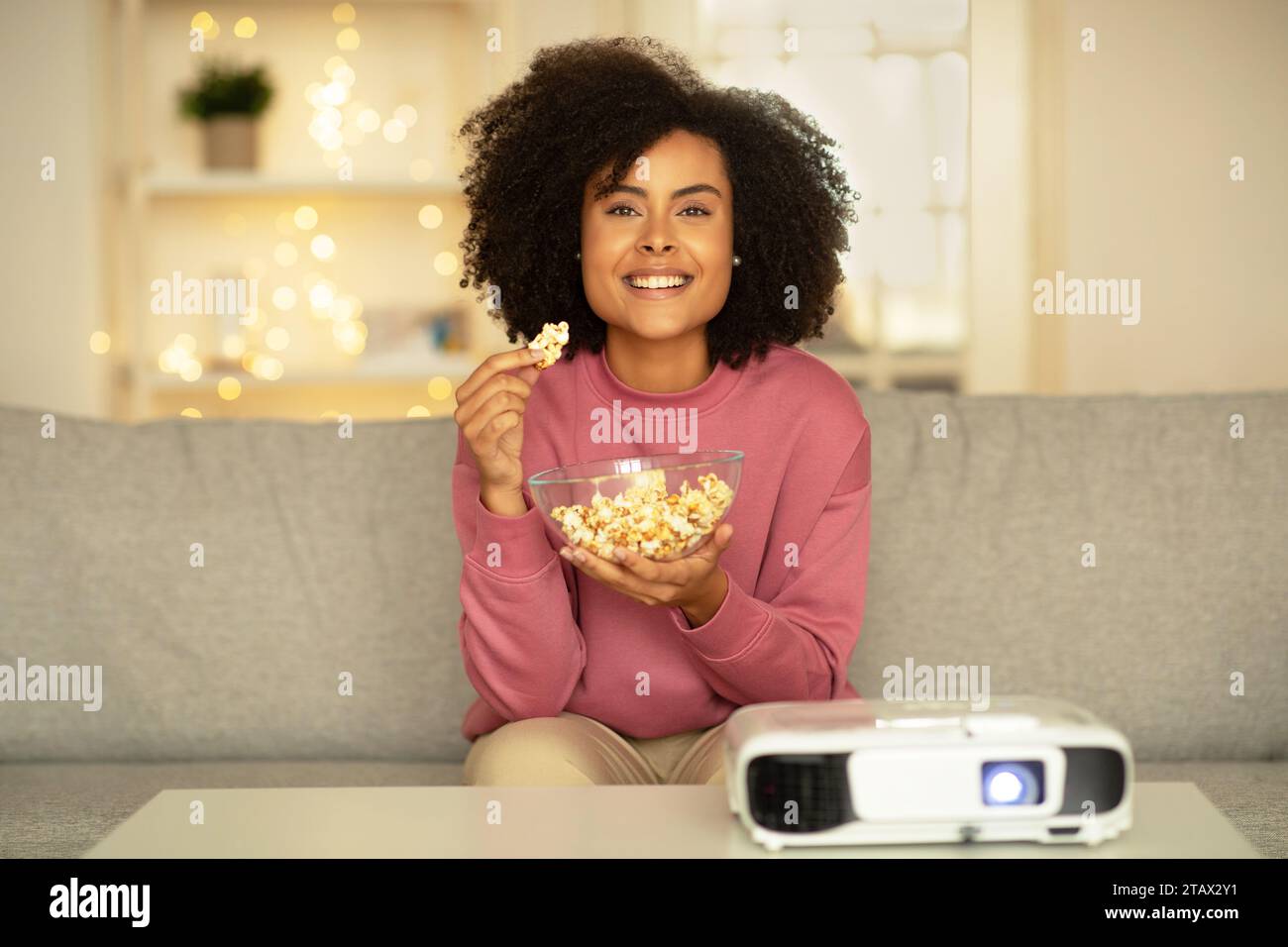 African American woman watches film on projector with popcorn indoor ...