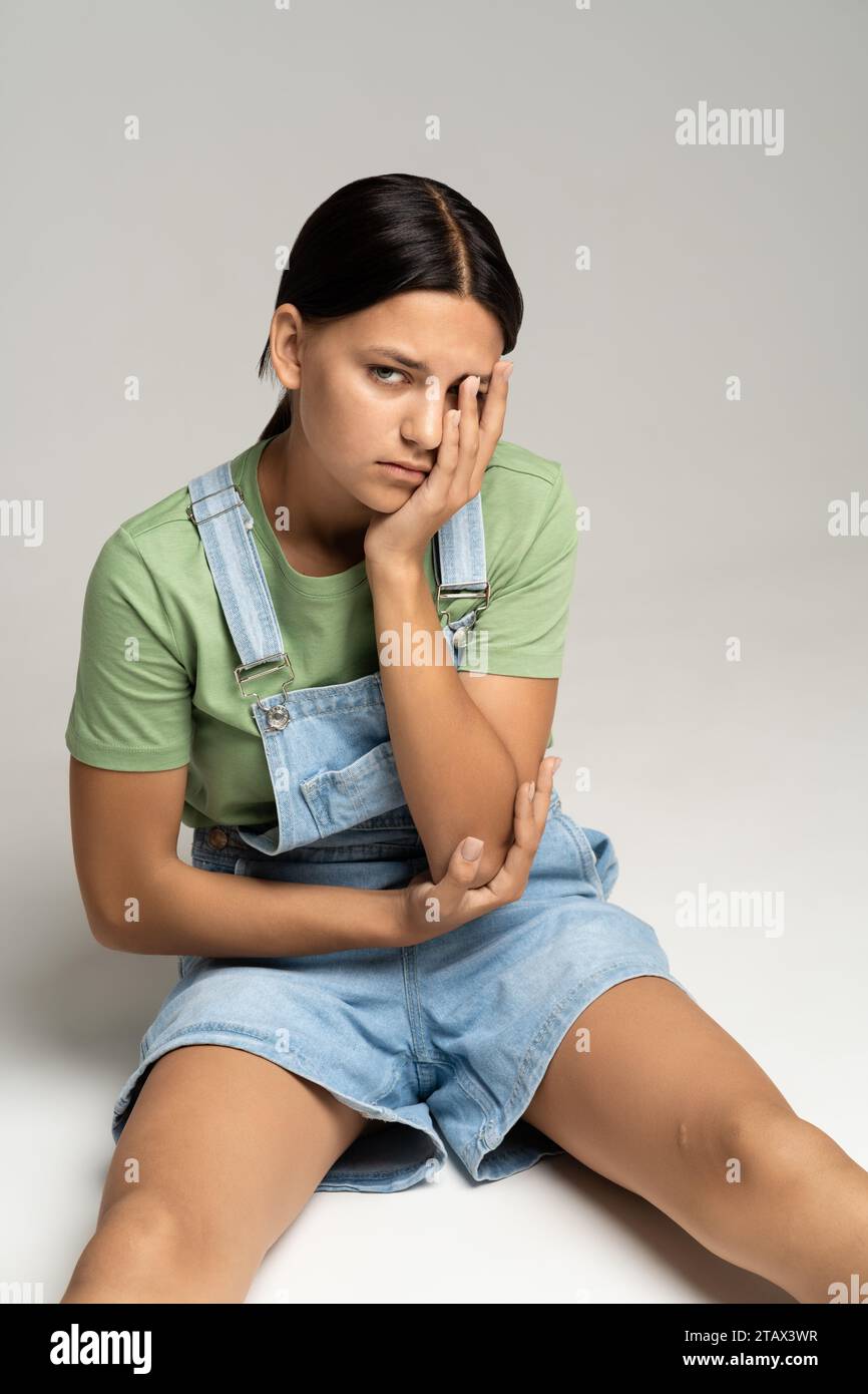 Boring brunette tan teen girl sitting on gray background looking at ...
