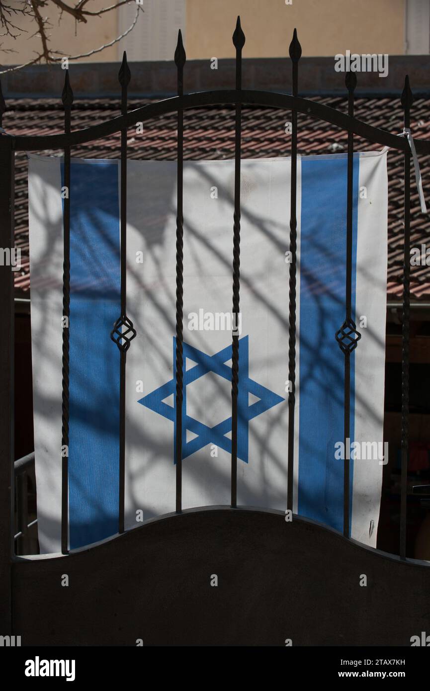 An Israeli flag hangs behind the rails of a decorative, metal fence in ...