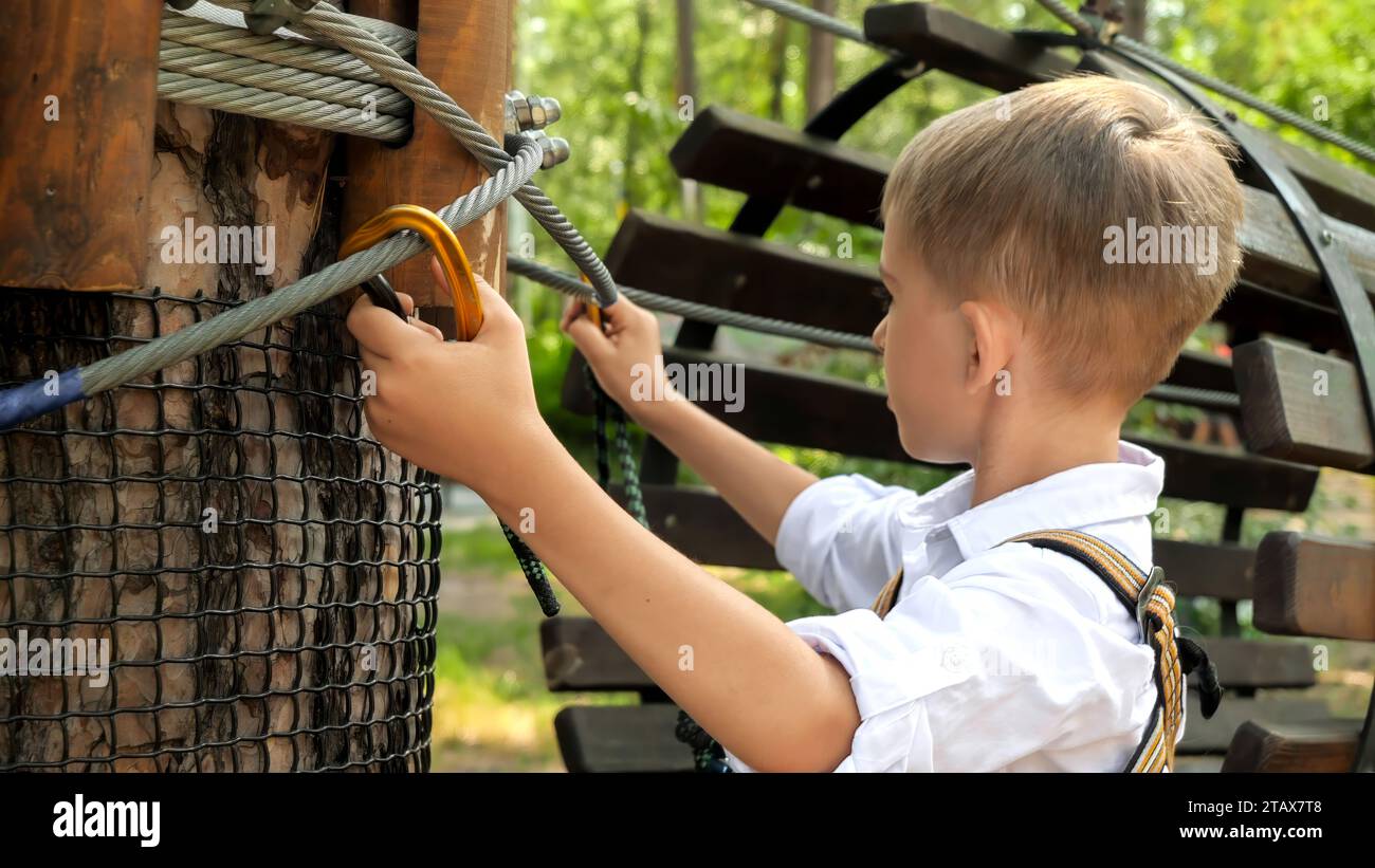 Portrait of little boy clamping his safety rope hook while climbing at ...