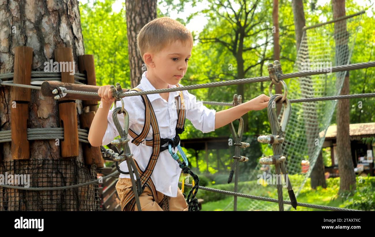 Portrait of cute little boy walking on the rope bridge while having fun ...