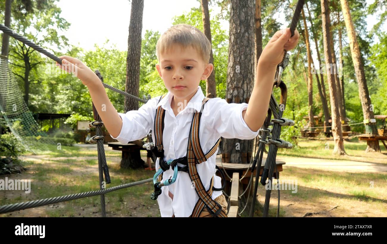 Little boy with safety rope walking over the wooden bridge strung in ...