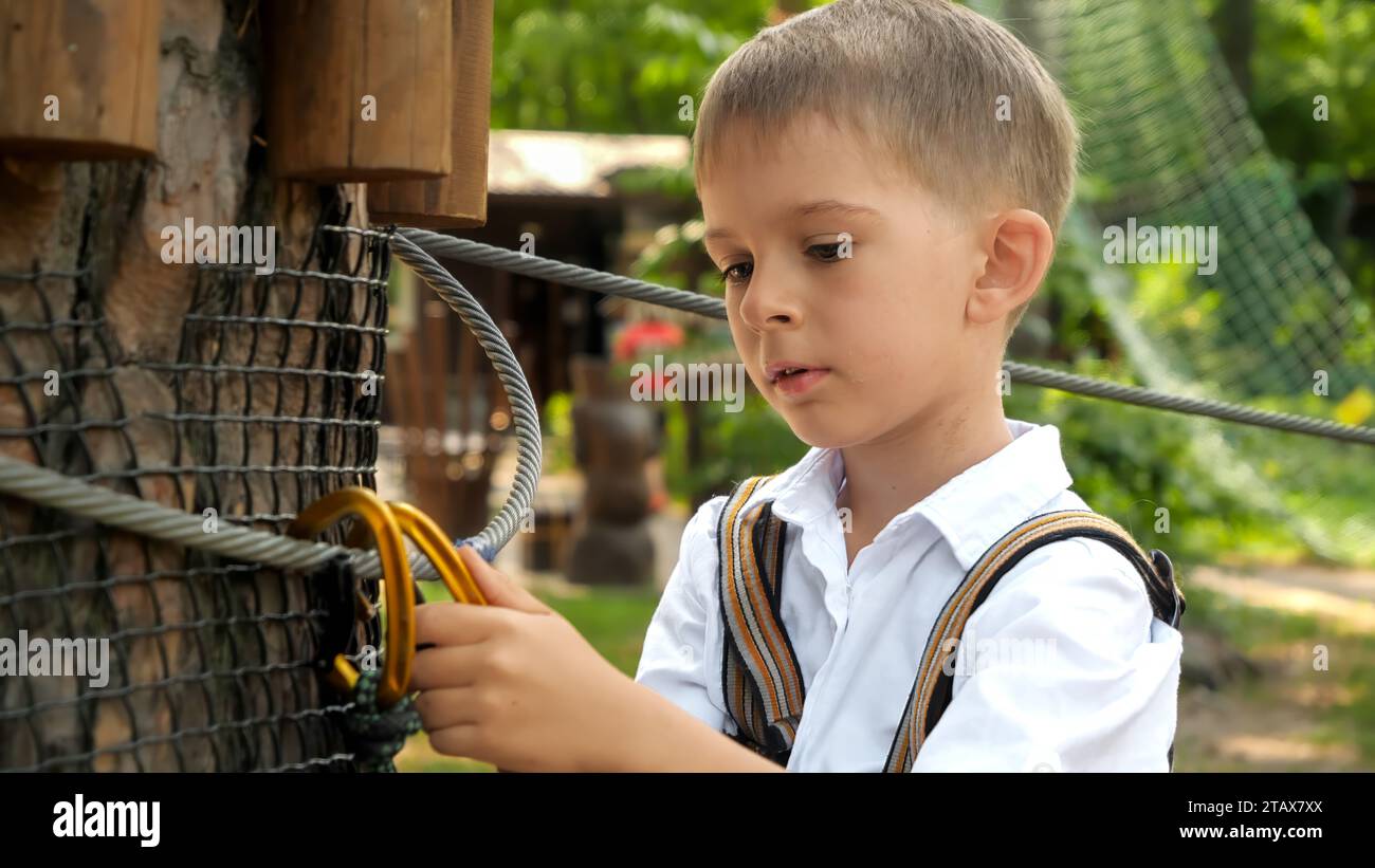 Little boy adjusting safety rope and hook in rope adventure park ...