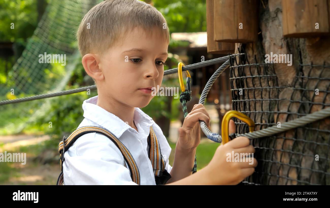 Portrait of little boy hooking his safety rope while climbing at ...