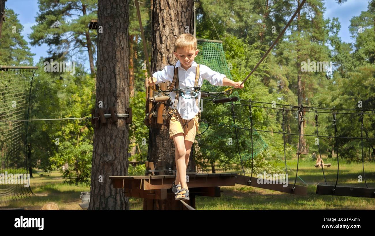 Boy holding by rope while walking on cable between two trees. Active ...