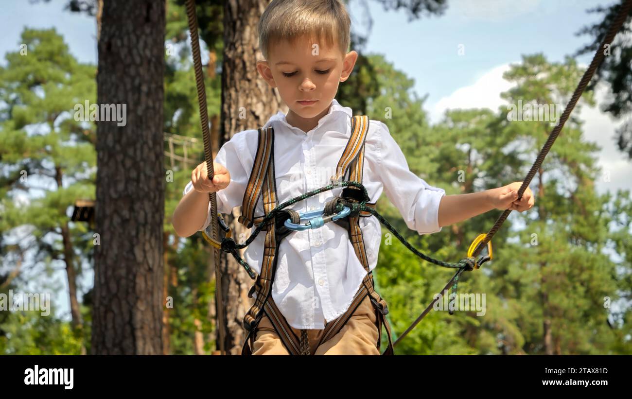 Portrait of boy tied with a safety rope walking up high on bridge ...