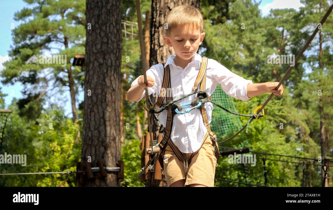 Portrait of little boy walking over rope strung between trees in scout ...