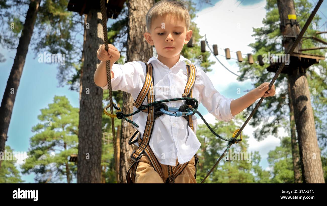 Portrait of little boy smiling while walking over strung rope in ...