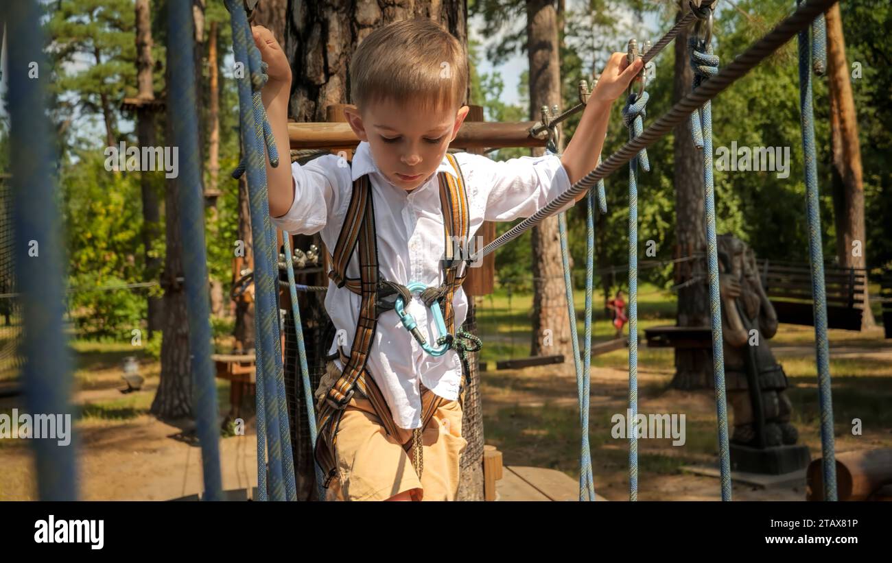 Little boy holding rope while crossing bridge strung between two trees ...