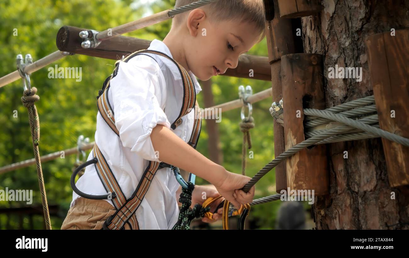 Little boy clamping safety rope hooks to the tree while climbing in ...