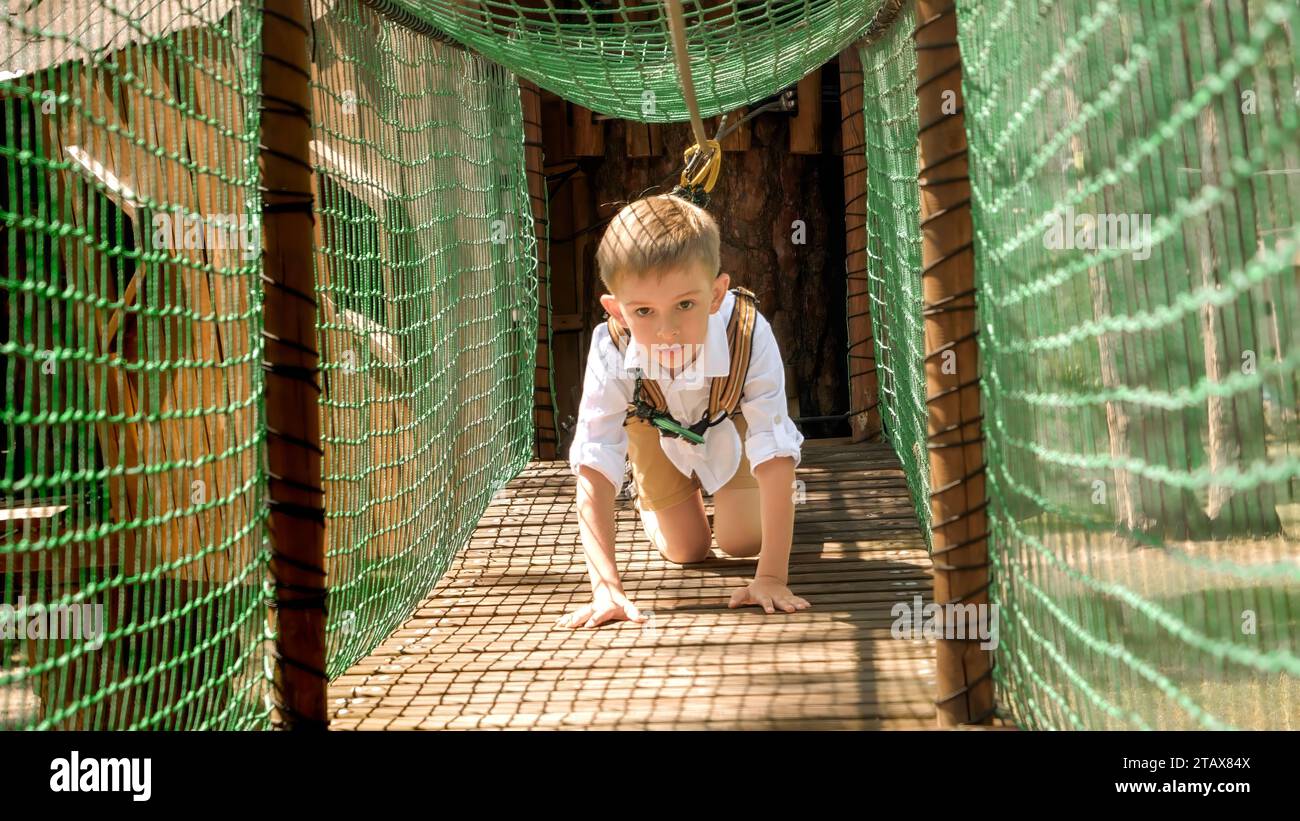 Little boy crawling on all fours over wooden bridge at rope adventure ...