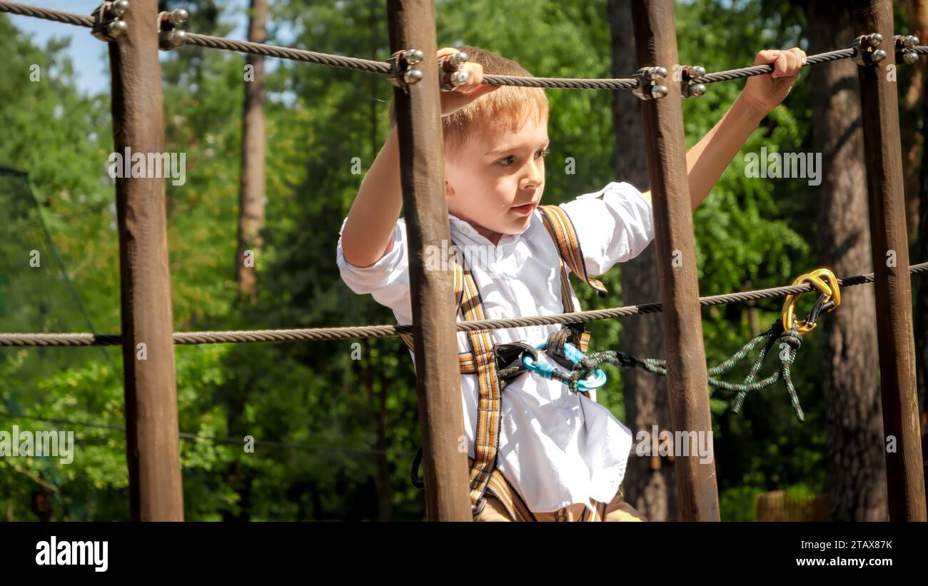 Portrait of little boy climbing over obstacles while having fun in rope ...