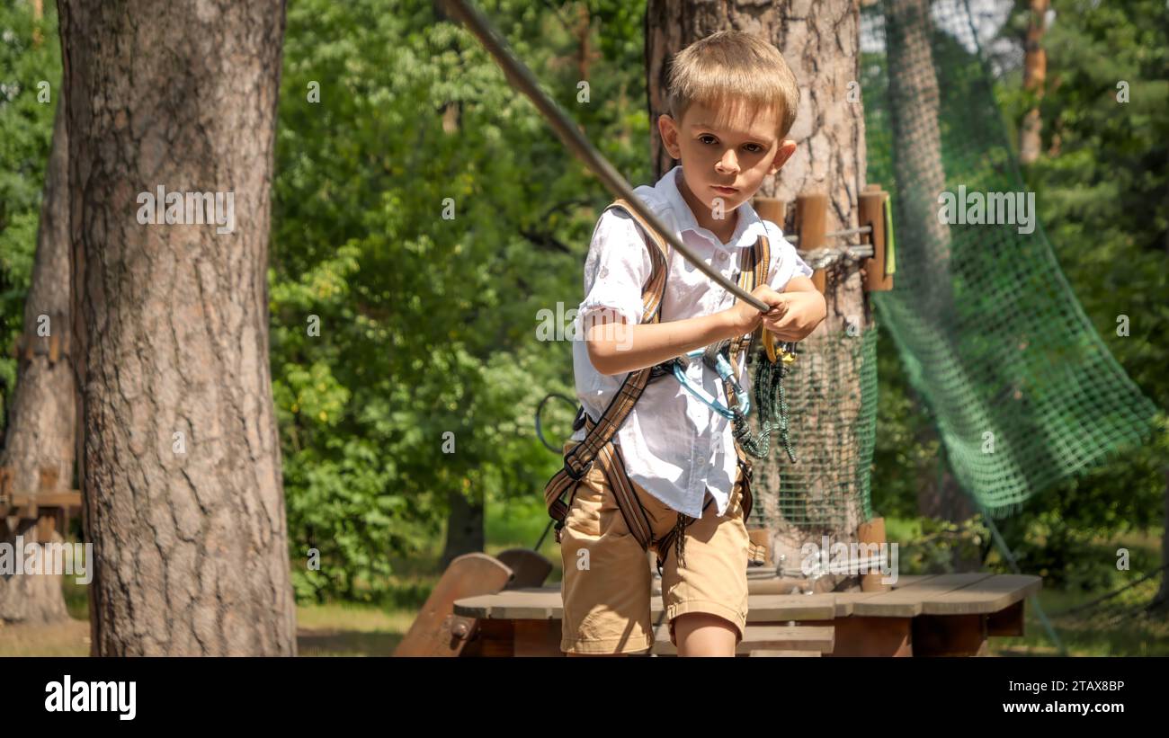 Portrait of little boy walking over strung rope between trees in ...