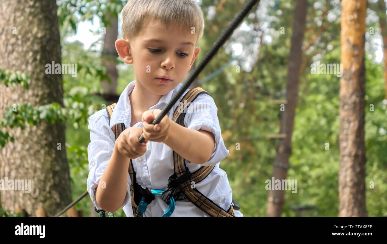Portrait of little boy holding tight rope while crossing obstacles at ...