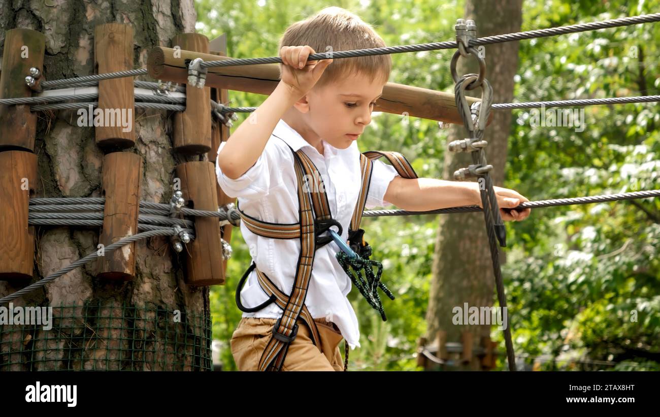 Portrait of brave boy walking over obstacles at rope park in forest ...