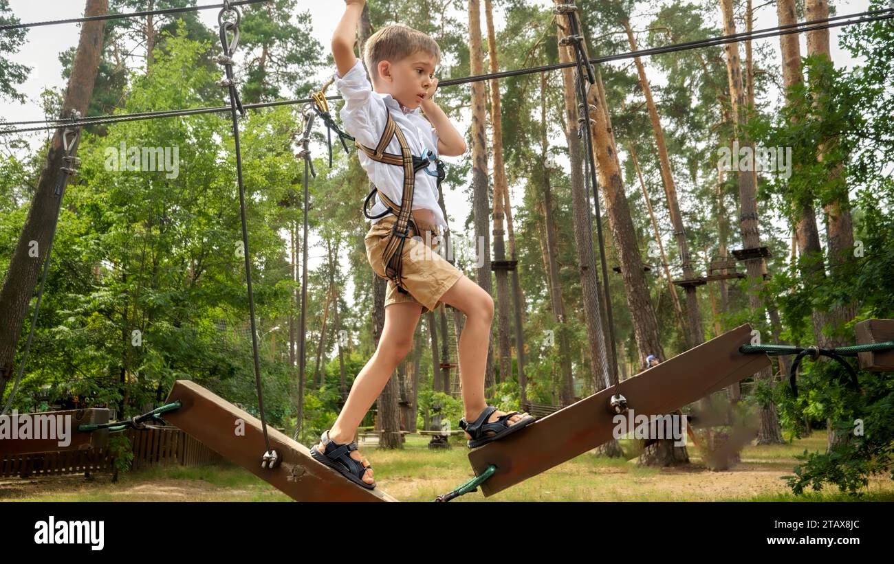 Little boy crossing wobbly suspension bridge at extreme adventure park ...