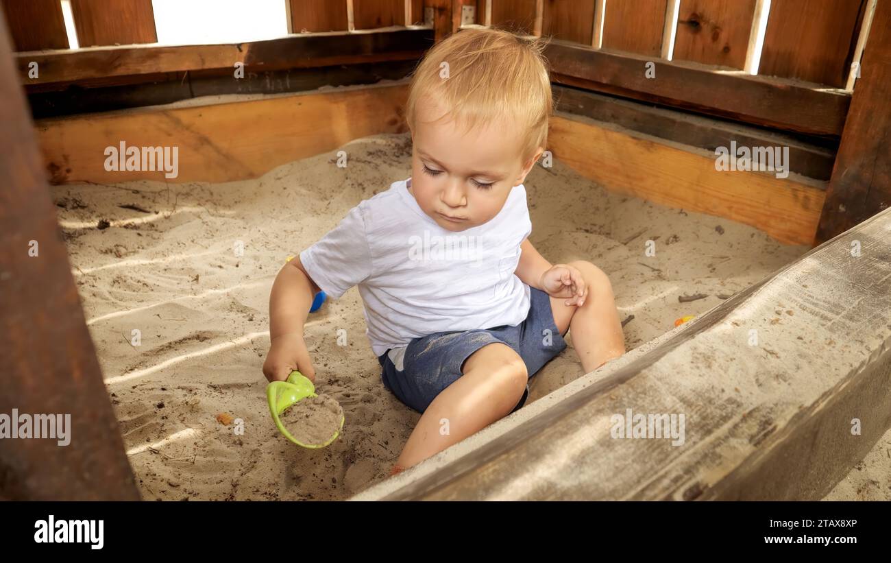 Cute little boy digging sand with toy shovel in sandbox at park. Kids ...