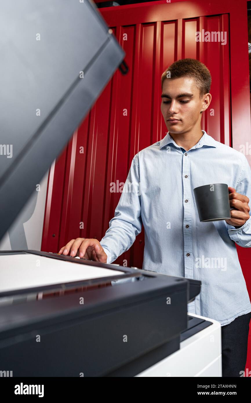 Positive young man using printer in the modern office Stock Photo - Alamy