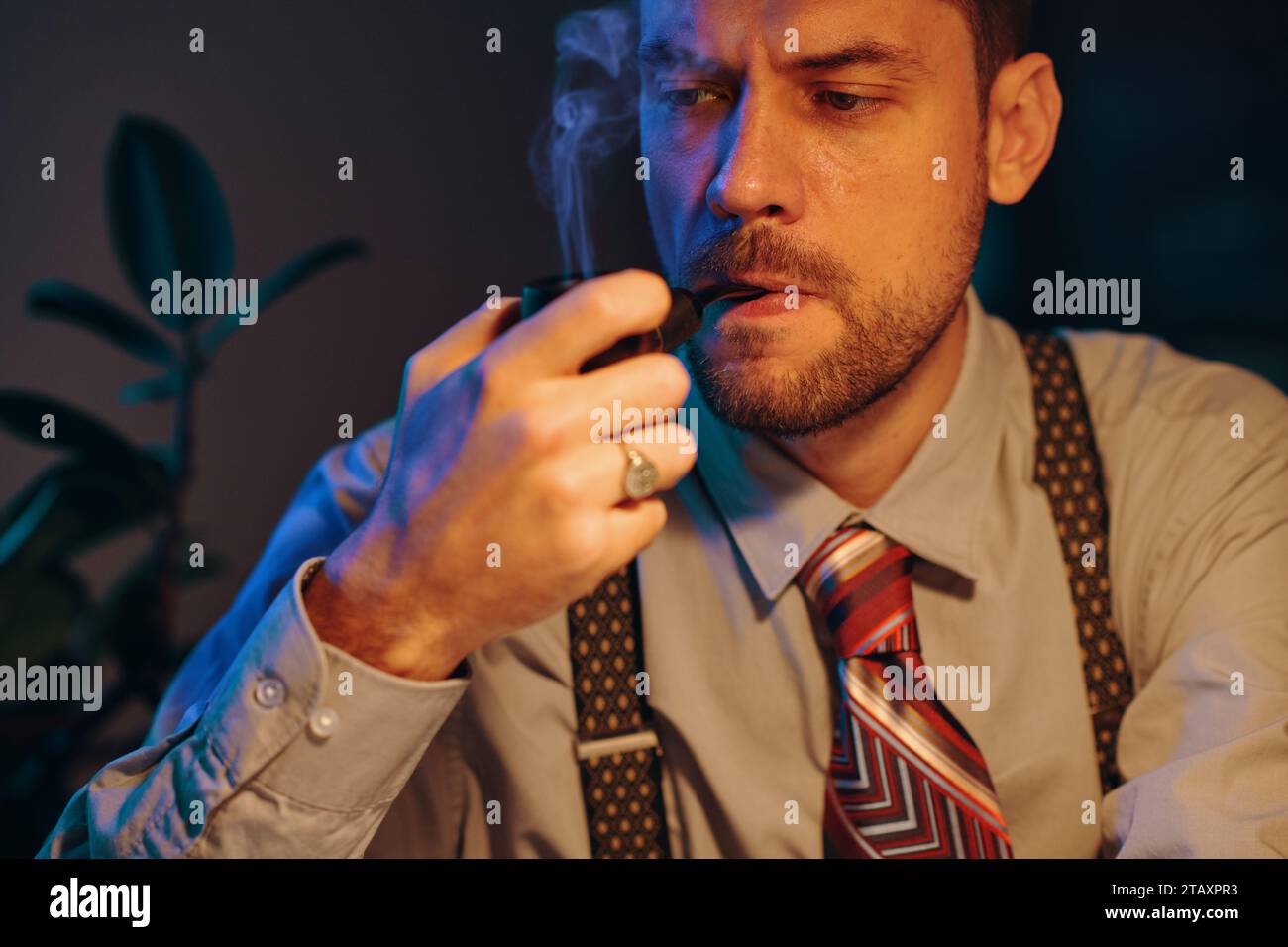 Young pensive businessman with smoking pipe in mouth sitting in front ...