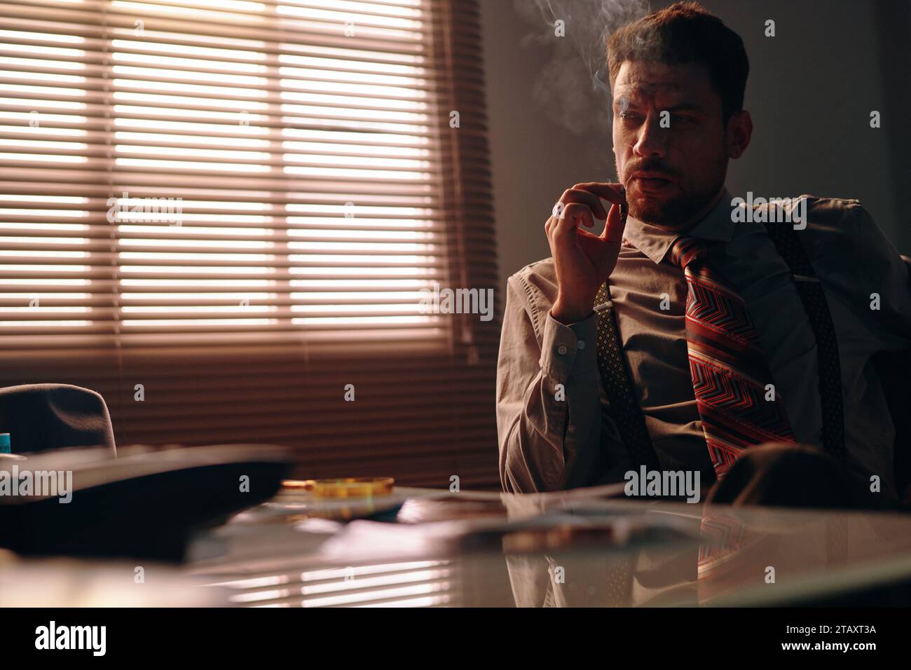 Young serious businessman in formalwear smoking cigarette while sitting ...