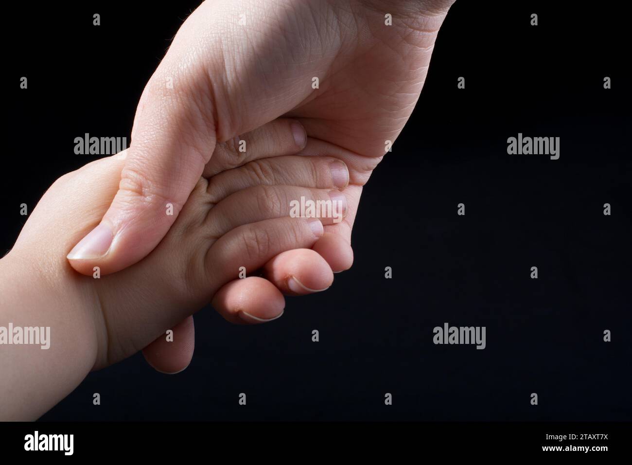 Adult and child hold hands in black background Stock Photo - Alamy
