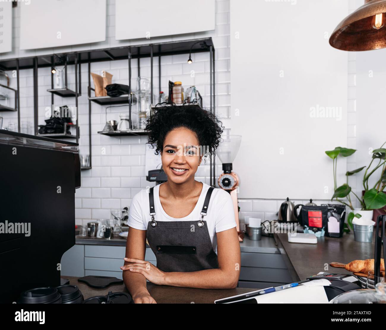 Waitress with curly hair in an apron standing at a counter in a cafe ...