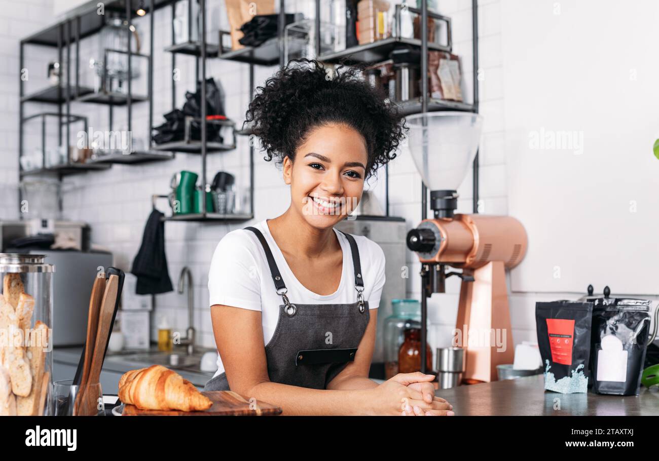Beautiful female barista looking at camera. Cheerful waitress in an ...