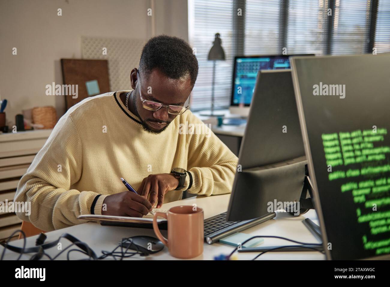 Software developer writing down plans for the day and ideas in notebook ...