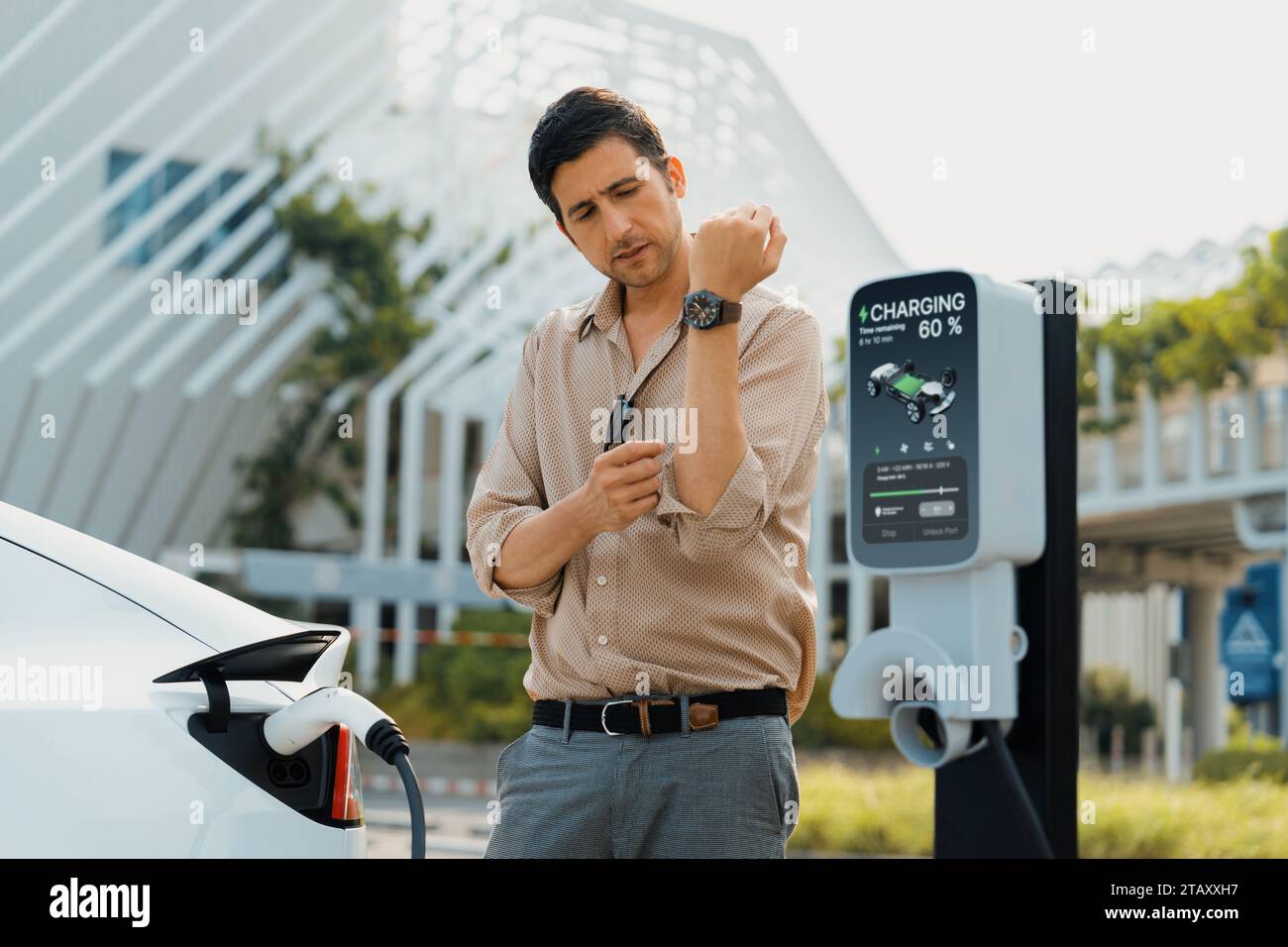 Young man checking time on smartwatch while EV charger to recharging ...