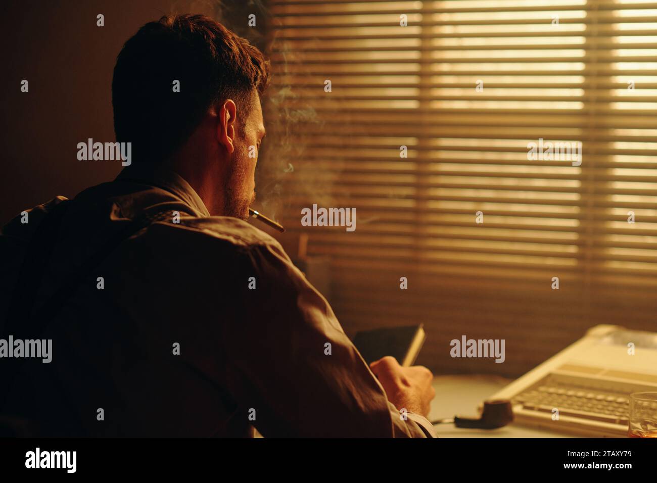 Back view of young man smoking cigarette and looking at book in his ...
