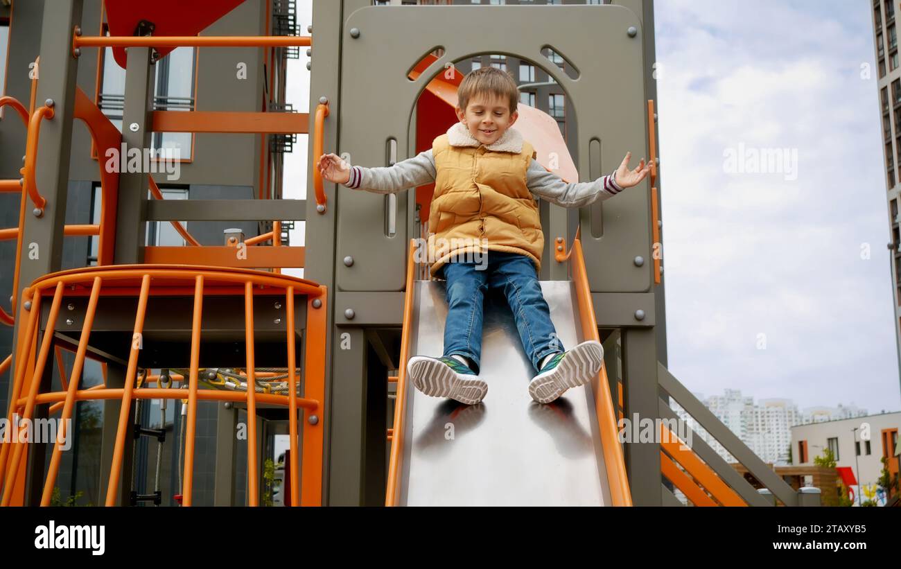 Little boy laughing as he slides down the slide on playground. Active ...
