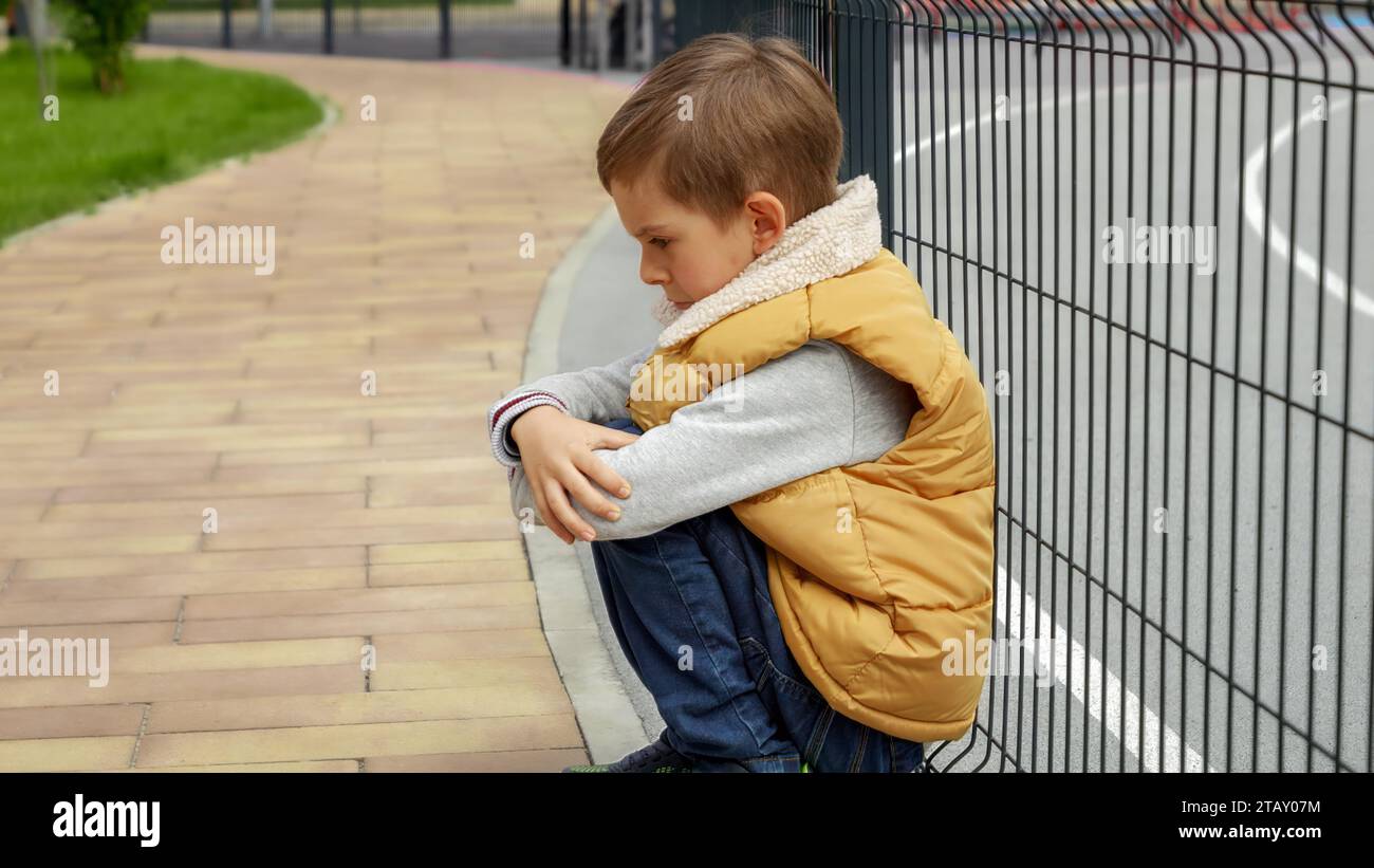 Unhappy lonely boy leaning on metal fence at school playground and ...