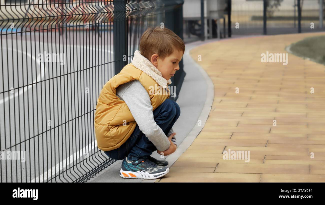 Little boy leaning on metal fence and sitting down. Child depression, problems with bullying ...