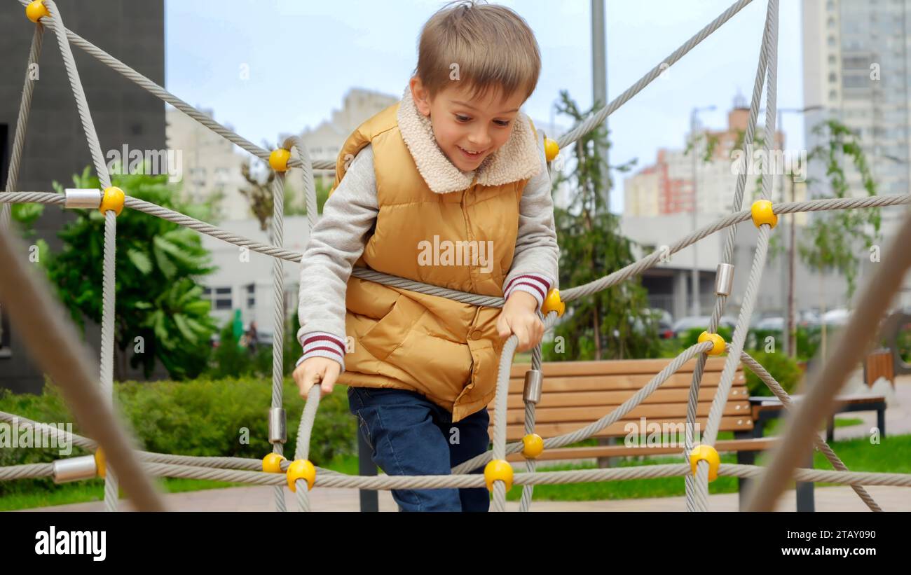 Curious smiling boy climbing and crawling through ropes and spider web ...