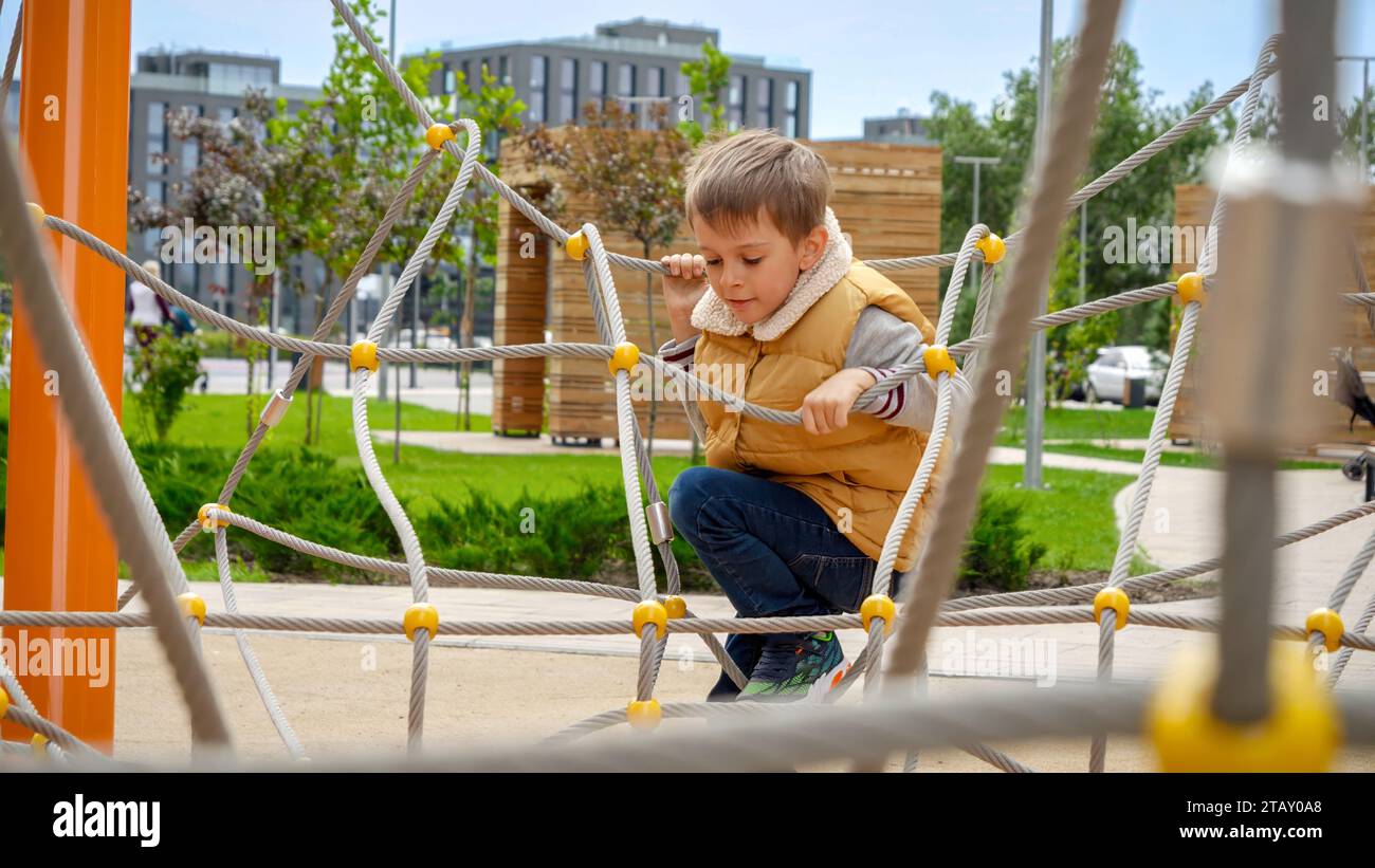 Little boy climbing through obstacles of ropes and nets on new public ...