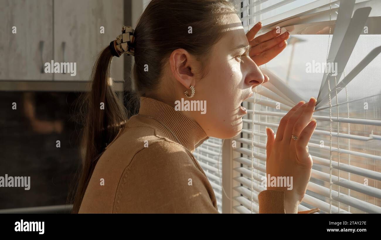 Scared woman saw crime on street through window blinds. Crime witness ...